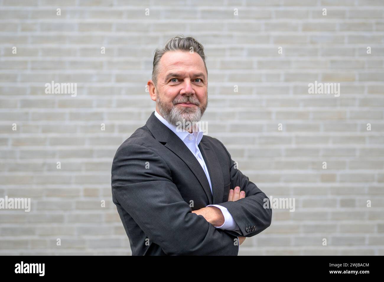 Shocked sixty year old gray man witg big eyes in front of a white brick ...