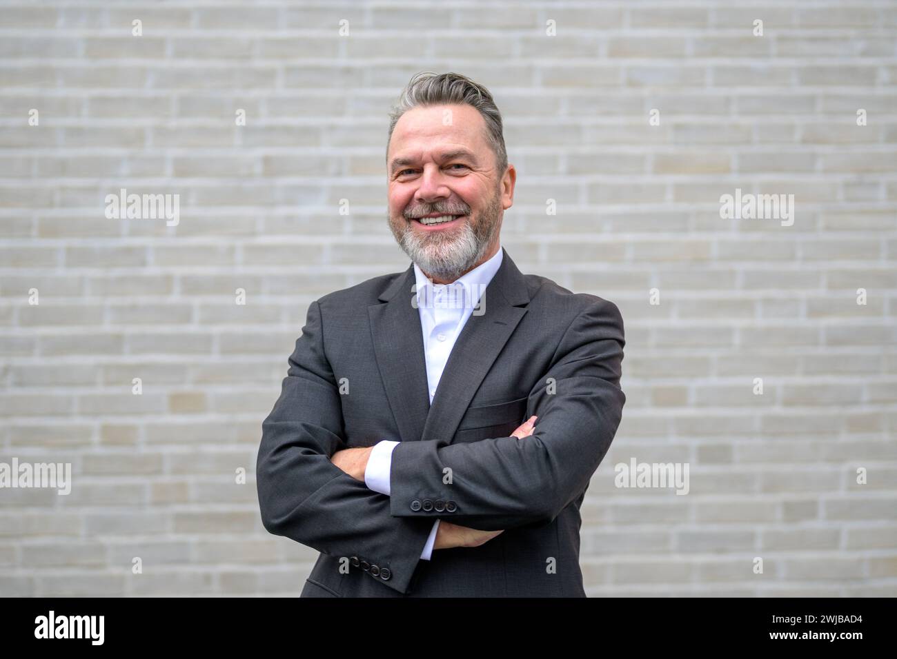 Happy sixty year old gray man in front of a white brick wall with his ...