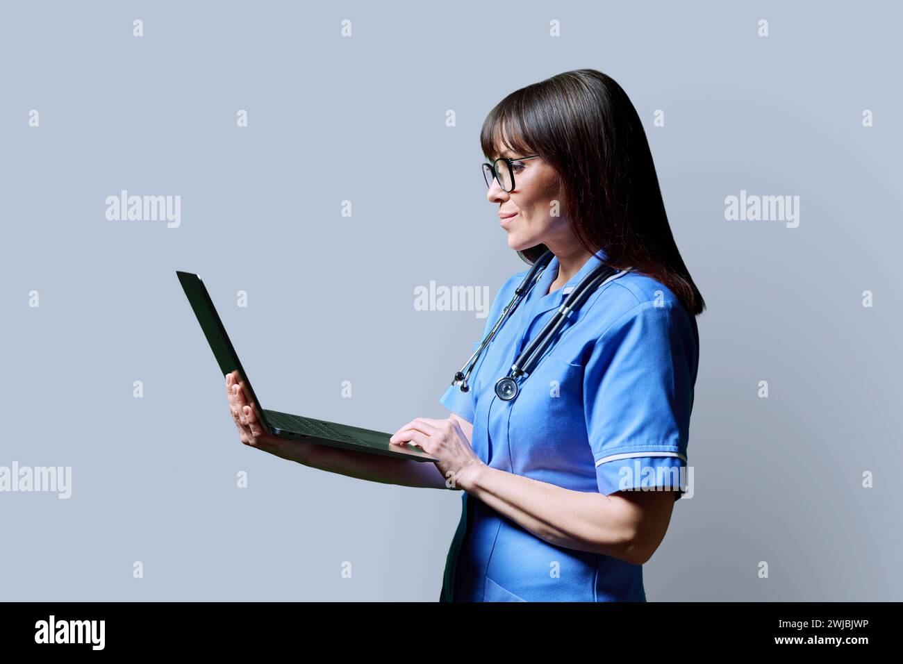 Female nurse using laptop, profile view on gray studio background Stock ...