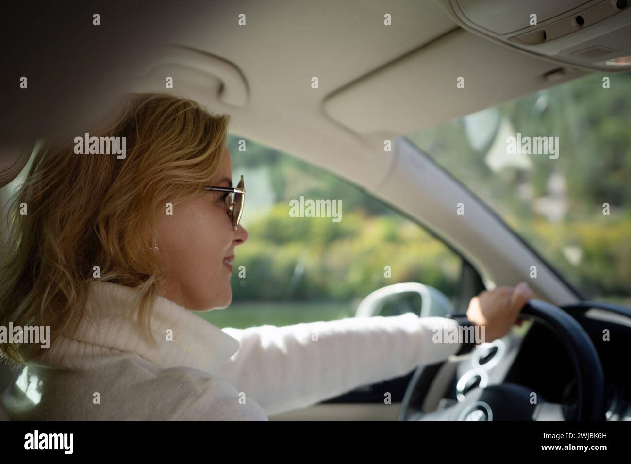 A blonde woman in a white sweater and jeans is driving. Happy woman ...