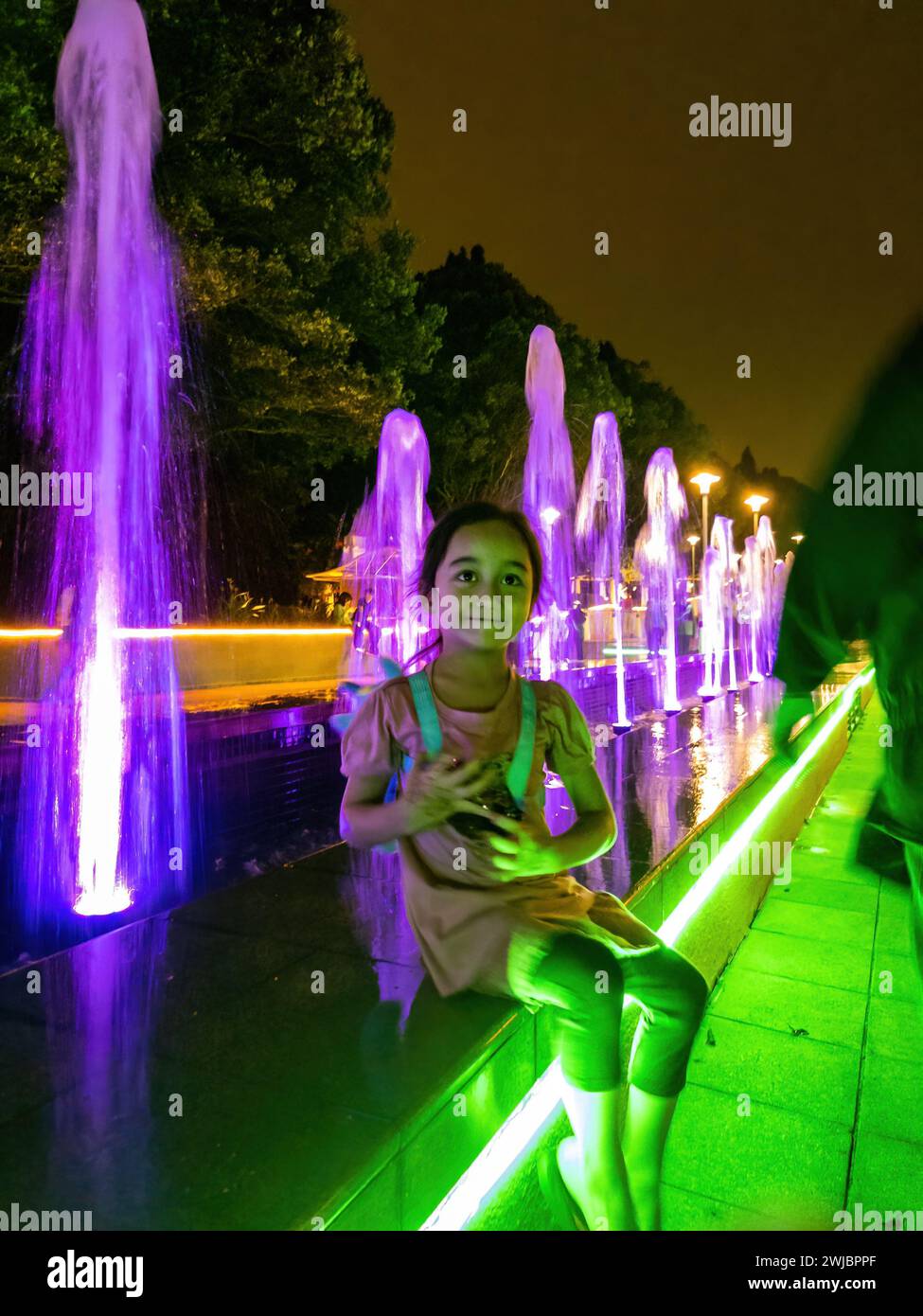 A young child is seated close to the nighttime LED-lit neon water ...