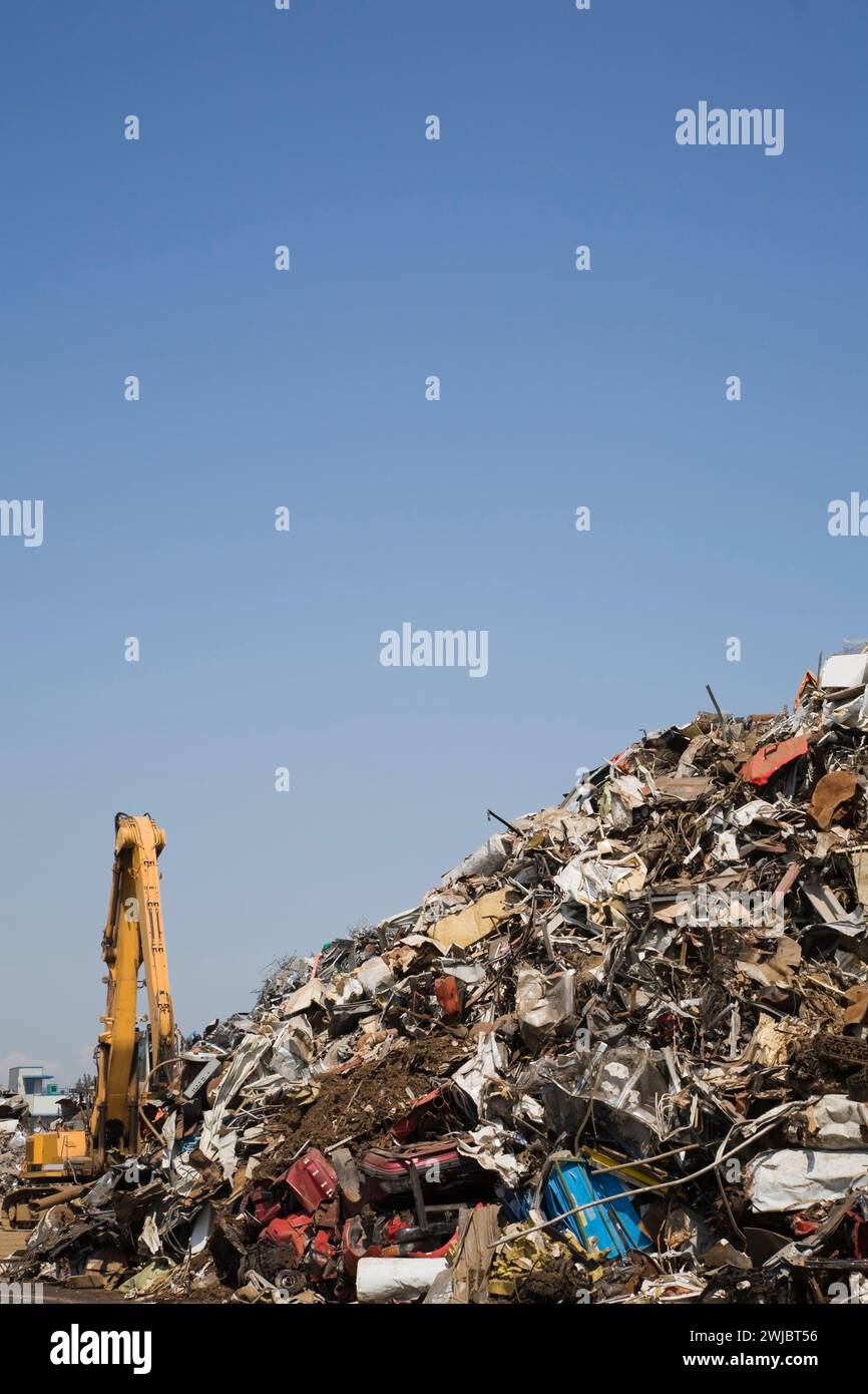 Crane loader with grappling arm next to pile of discarded household and ...