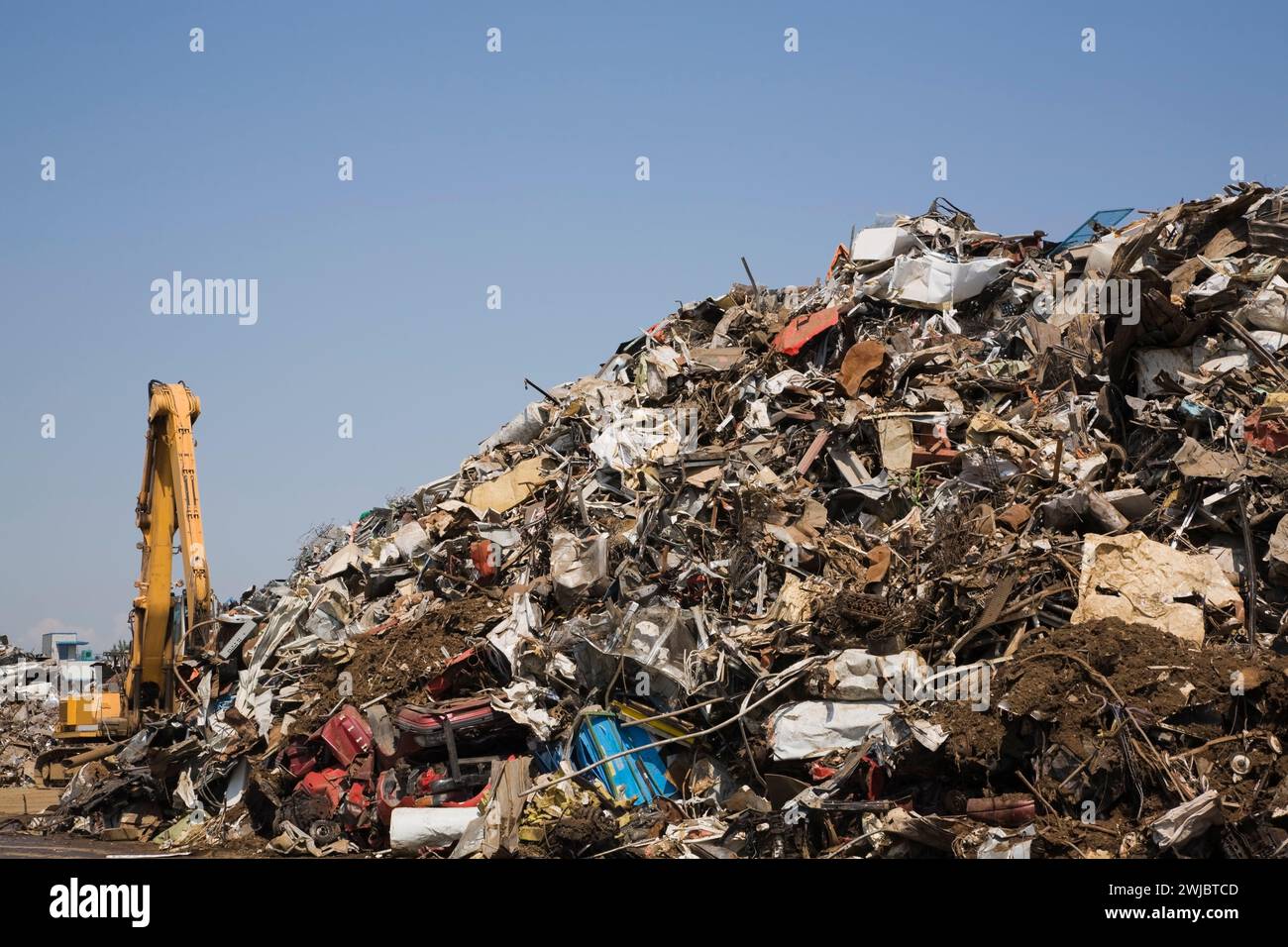 Crane loader with grappling arm next to pile of discarded household and ...