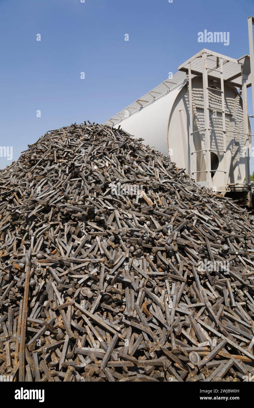 Pile of railroad spikes and tanker car at scrap metal recycling yard ...
