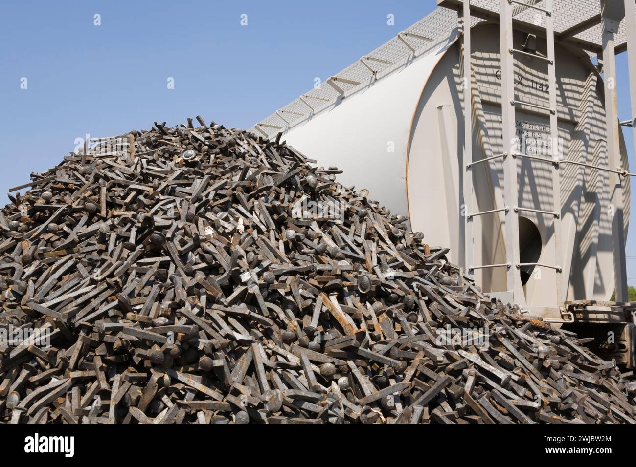 Pile of railroad spikes and tanker car at scrap metal recycling yard ...