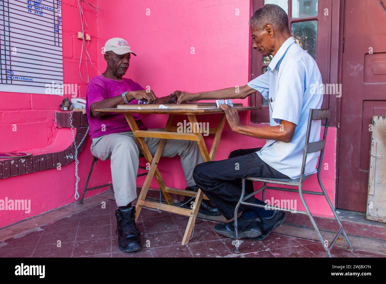Two older Dominican men playing a game of dominoes on the porch of a ...
