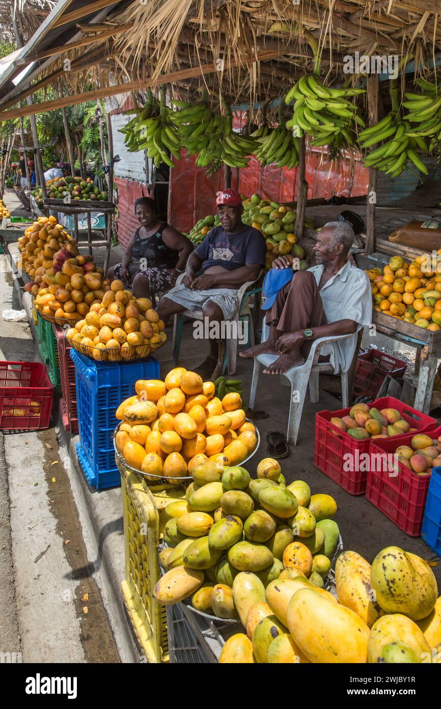 Three people selling mangos at a roadside fruit stand in Bani ...