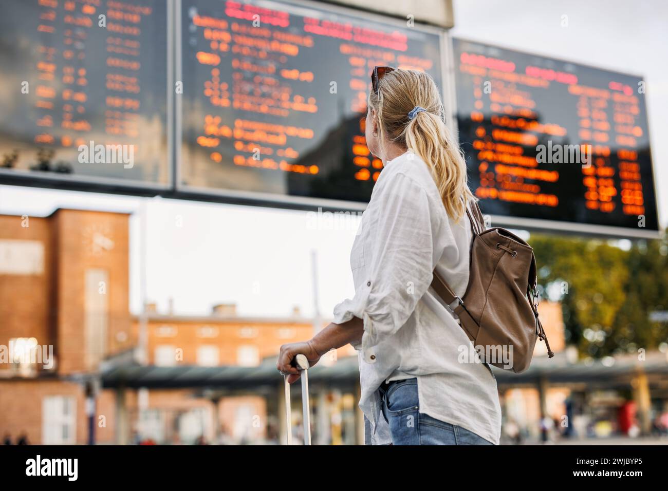 Woman passenger is checking arrival and departure board schedule ...
