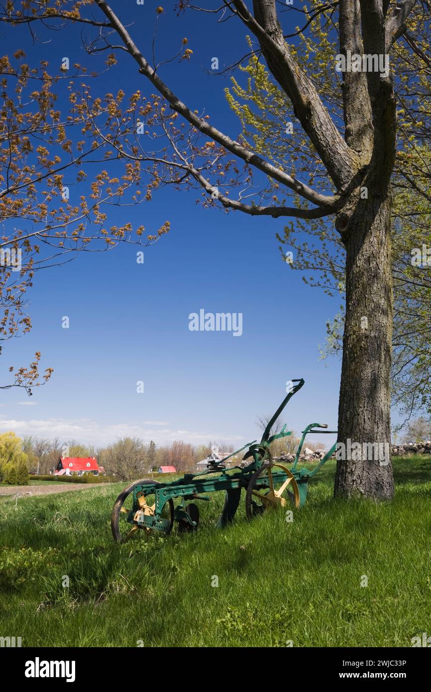 Old wrought iron manual plow next to tree and red Canadiana home in ...