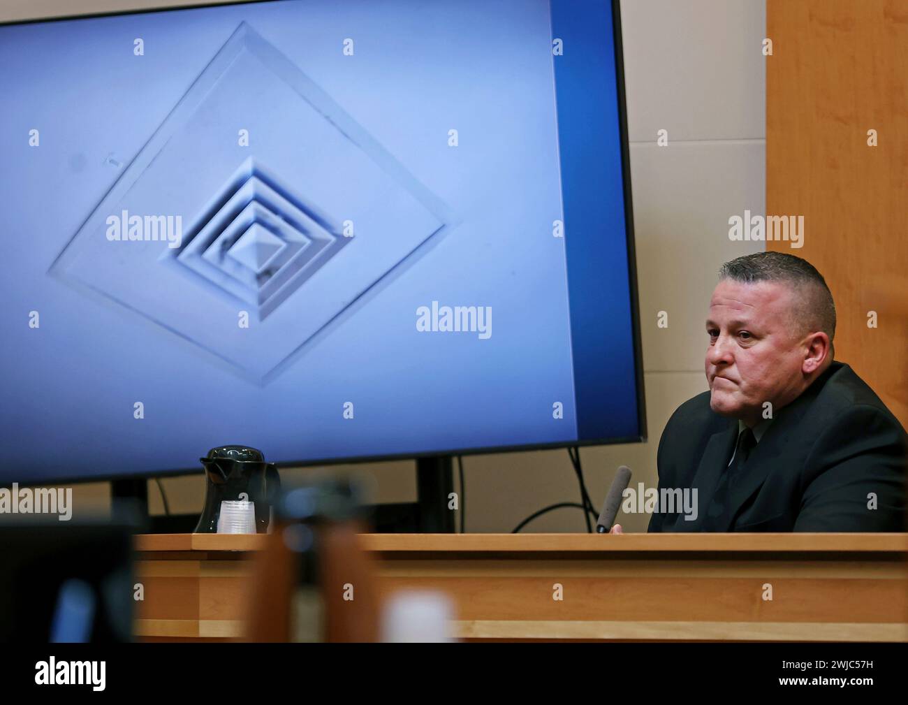 Scott Riley testifies in front of a photo of a vent on the ceiling of ...