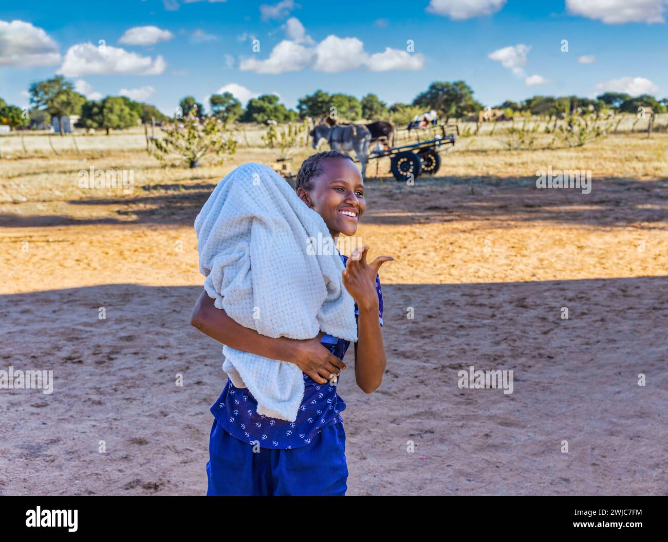 village african girl holding a baby, sandy area with a donkey cart in ...