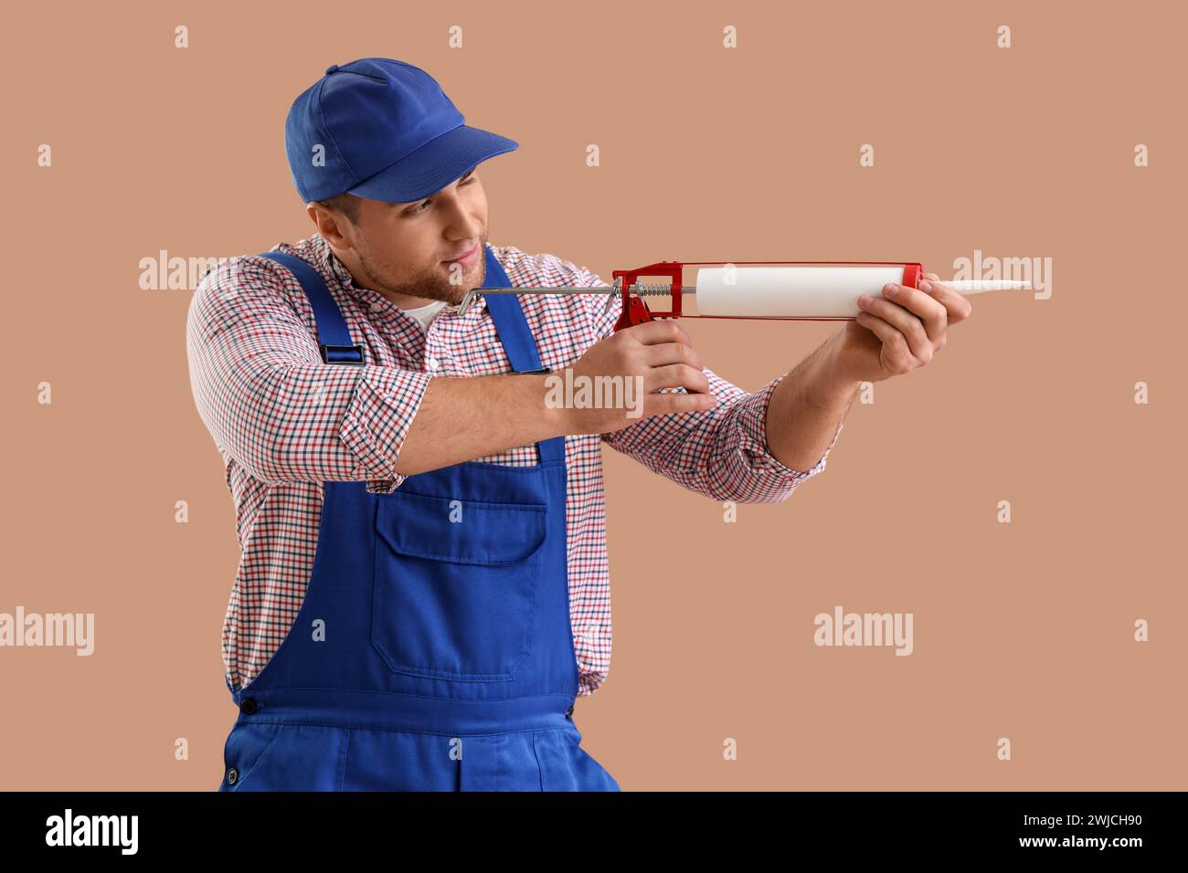 Male plumber with caulking gun on brown background Stock Photo - Alamy
