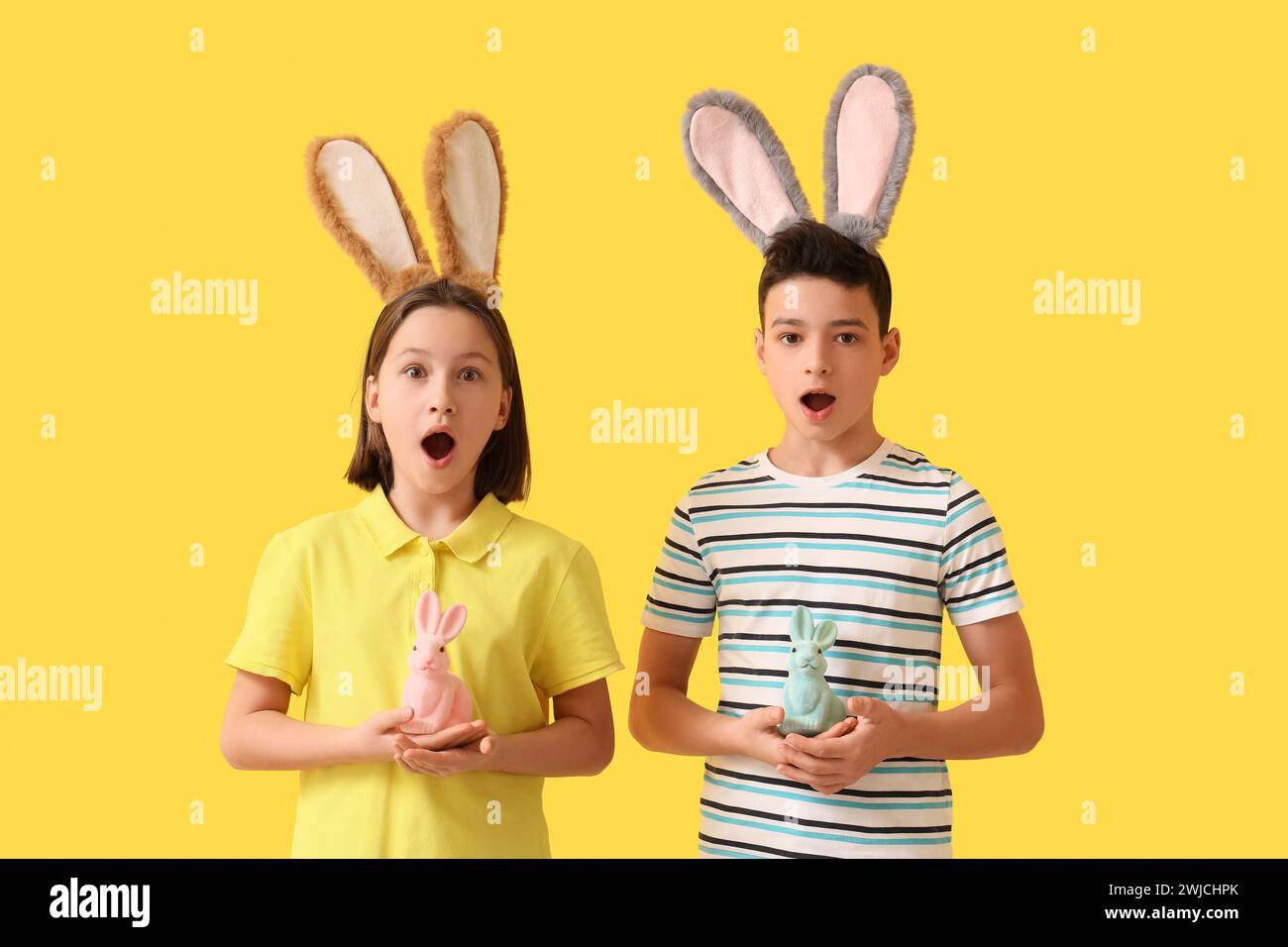 Shocked little children in bunny ears with Easter rabbits on yellow ...