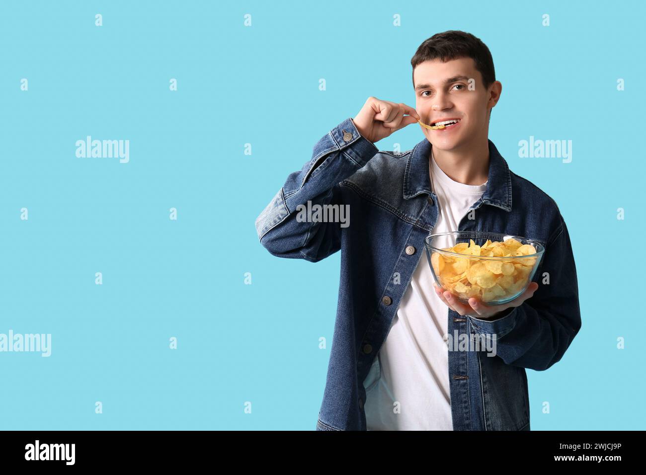 Young man eating potato chips on blue background Stock Photo - Alamy