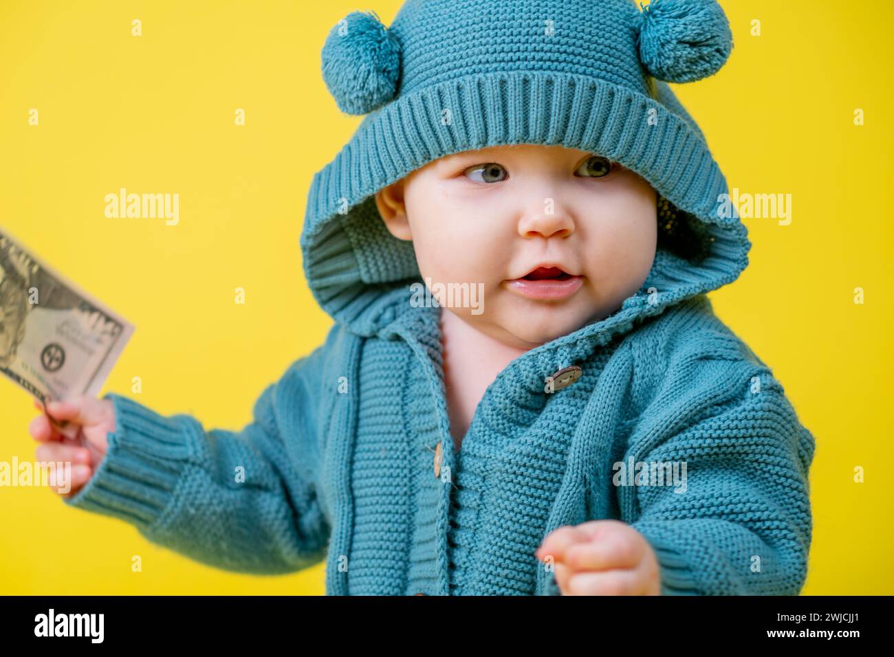 Baby in a blue knitted suit with money on a yellow background. Cute kid ...