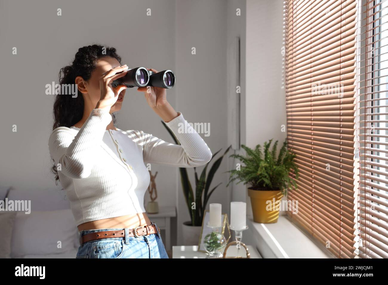 Young African-American woman looking through binoculars in window at ...