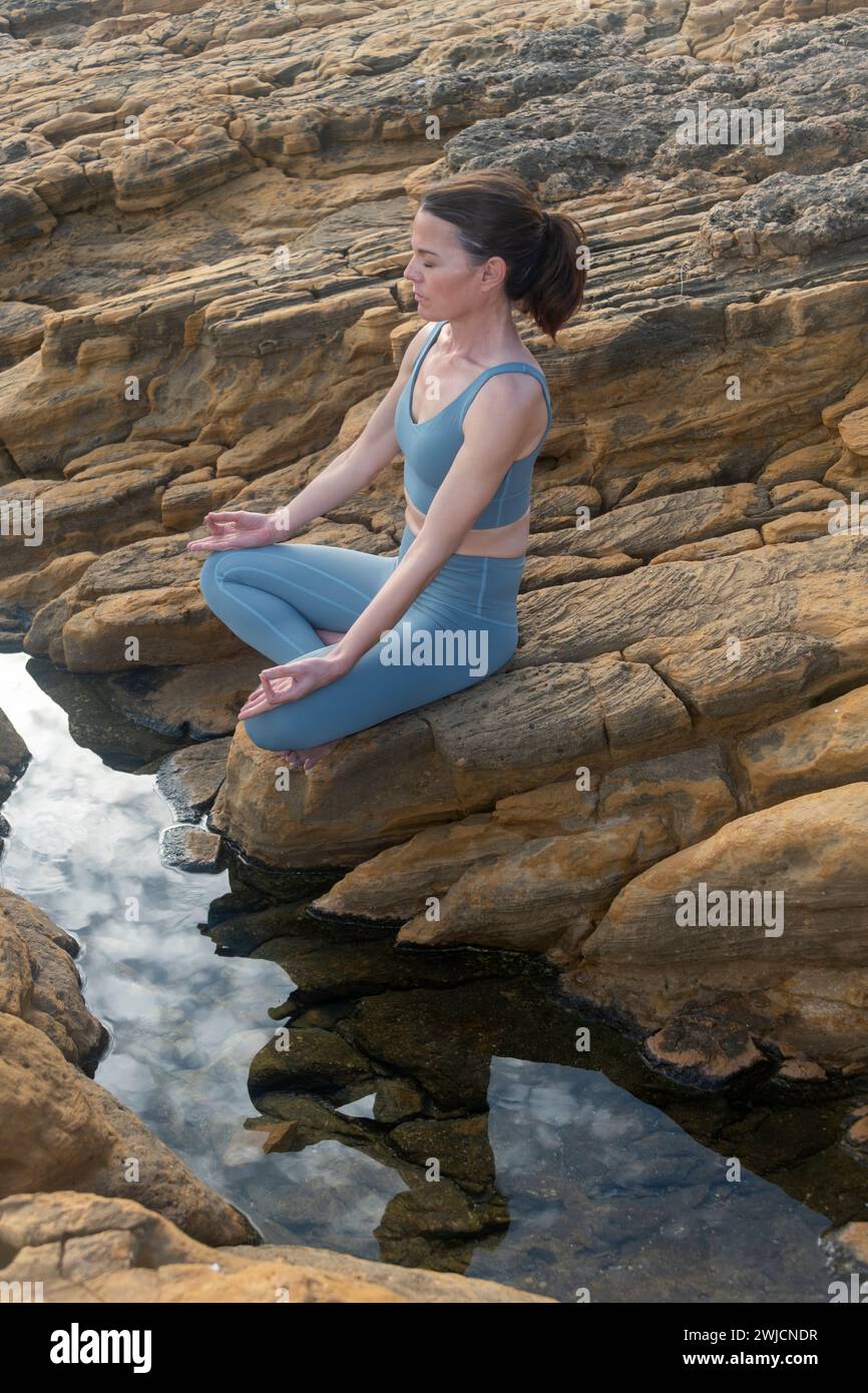 woman sitting on rocks meditating and practicing yoga, reflections in ...