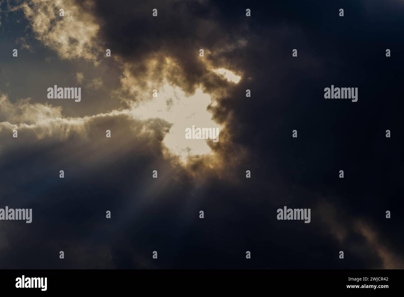 Dark clouds with sun in middle of frame breaking through sending rays ...