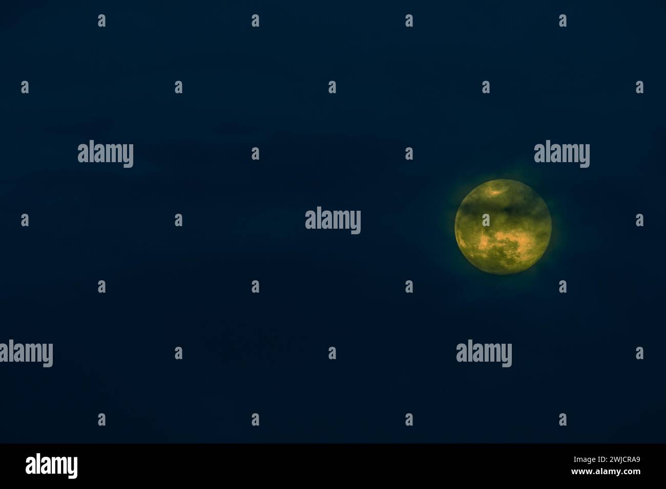 Bright yellow full moon behind clouds in a blue sky at blue hour just ...