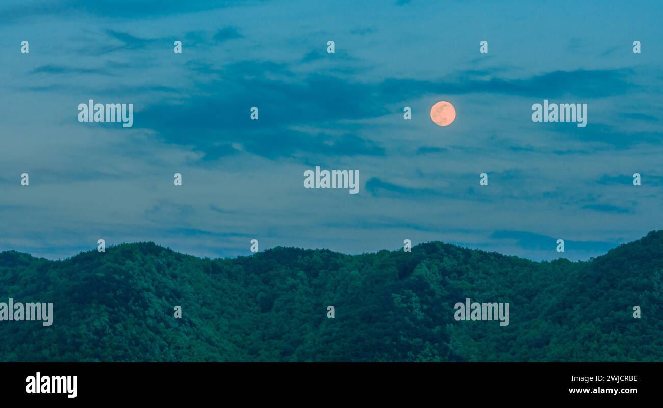 Full moon in blue sky with white clouds over mountains covered with ...
