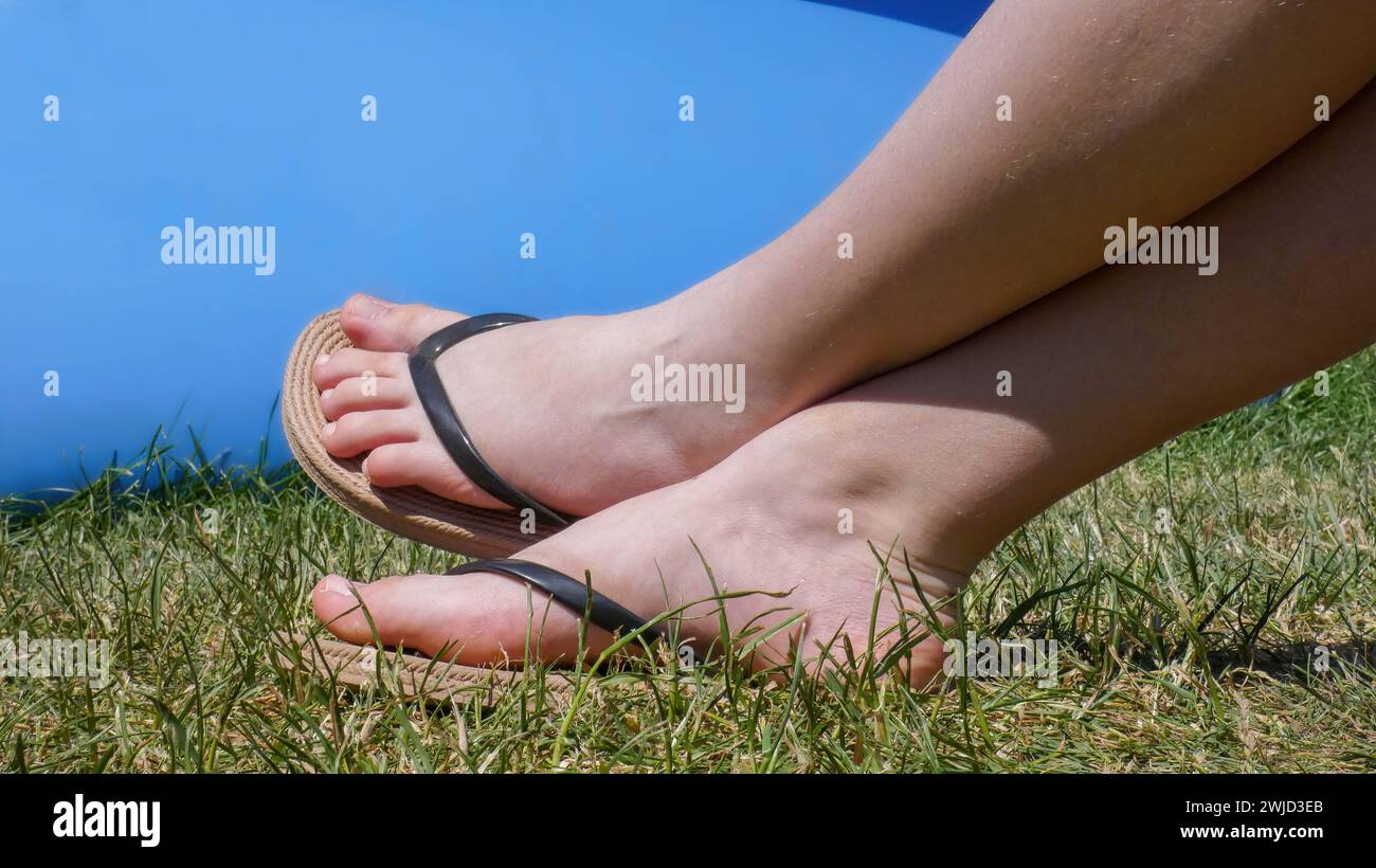 Legs of a sitting woman in green grass in the summer, by the pool, with ...