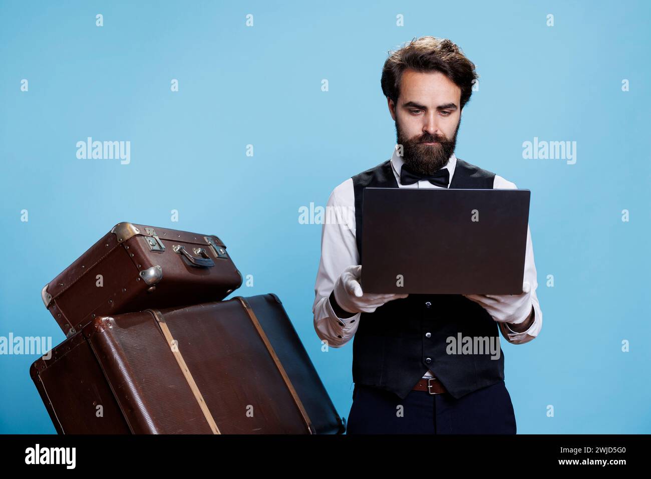 Hotel porter in suit using laptop against blue background, showcases ...