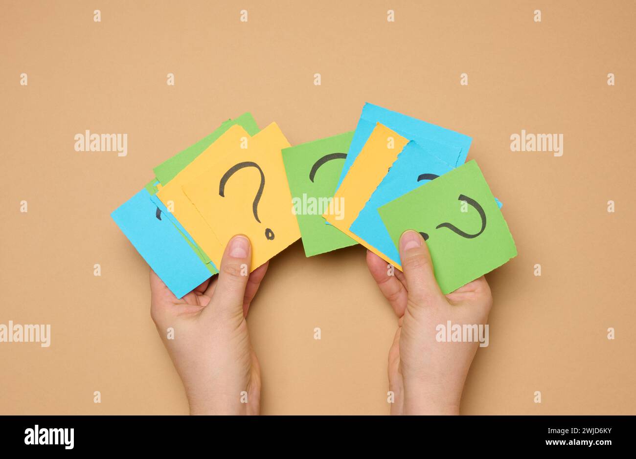 Female hands hold paper sheets with a drawn question mark on a beige ...