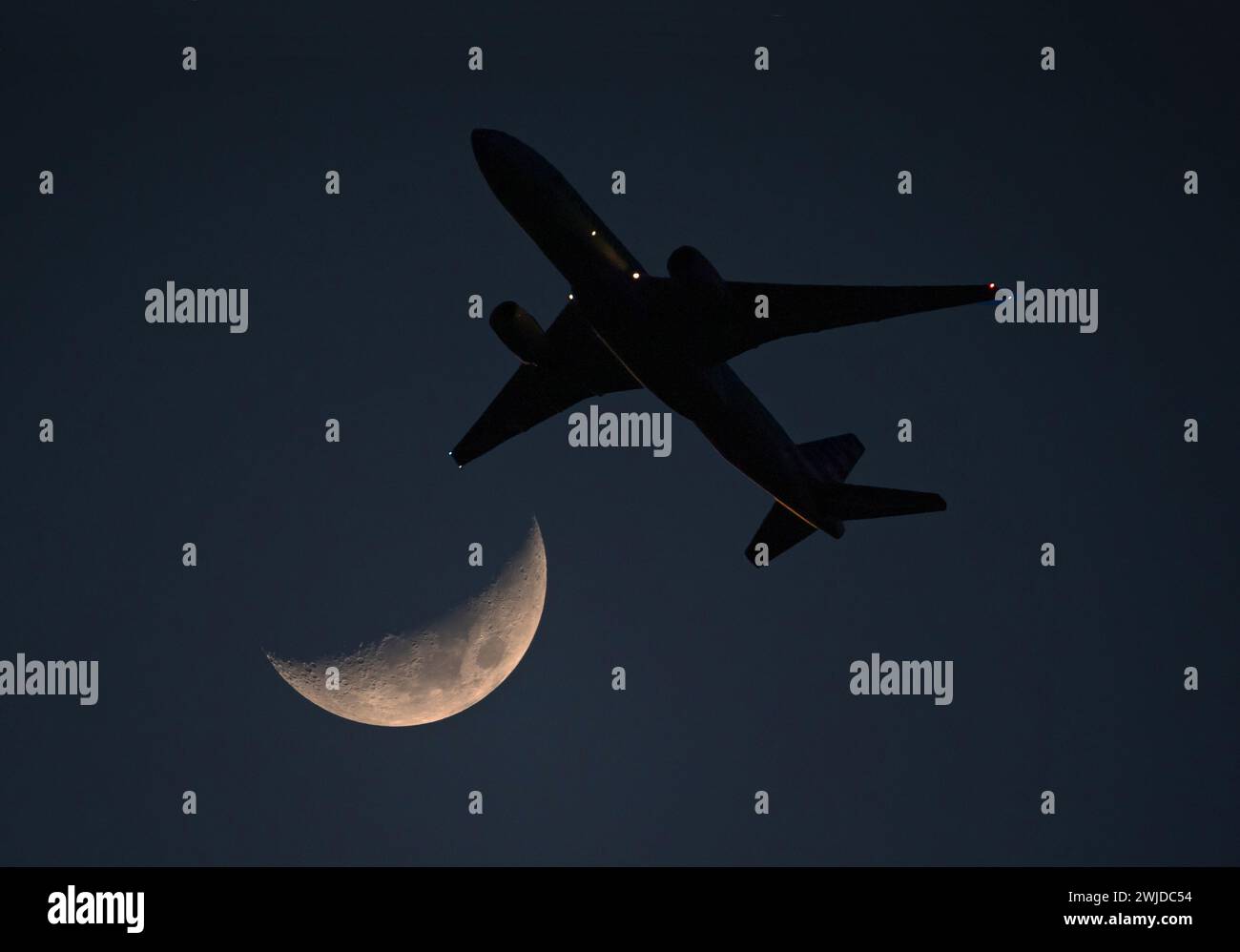 A commercial airliner shortly after take off passes by a crescent moon ...