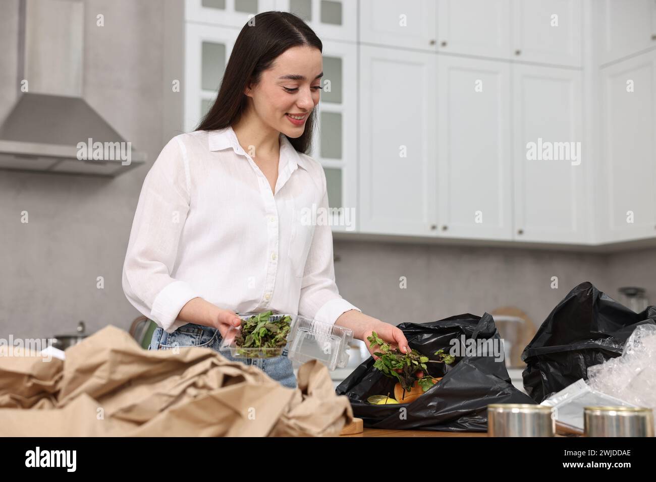 Garbage sorting. Woman putting food waste into plastic bag at table in ...