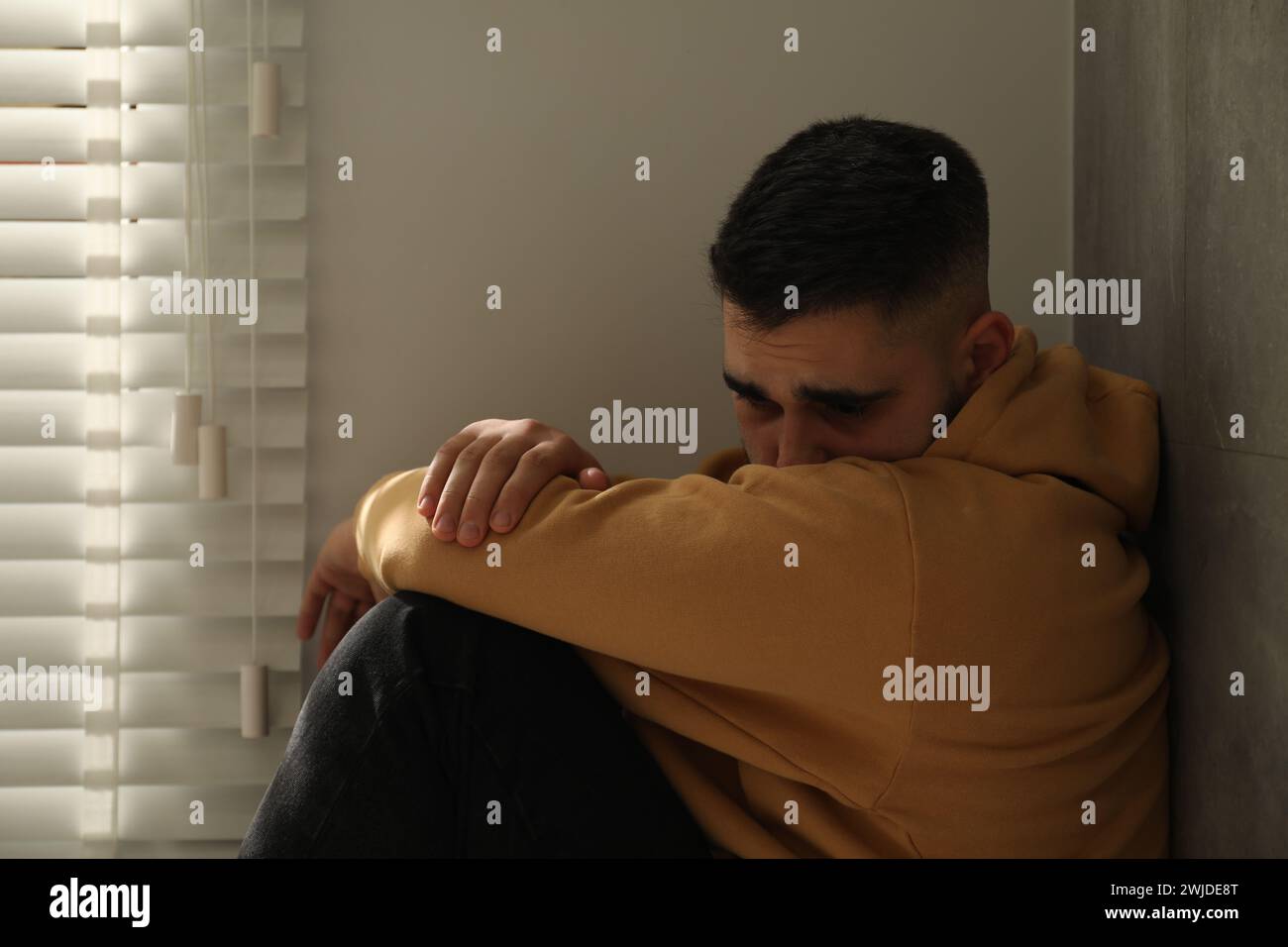 Sad man sitting near window at home Stock Photo - Alamy