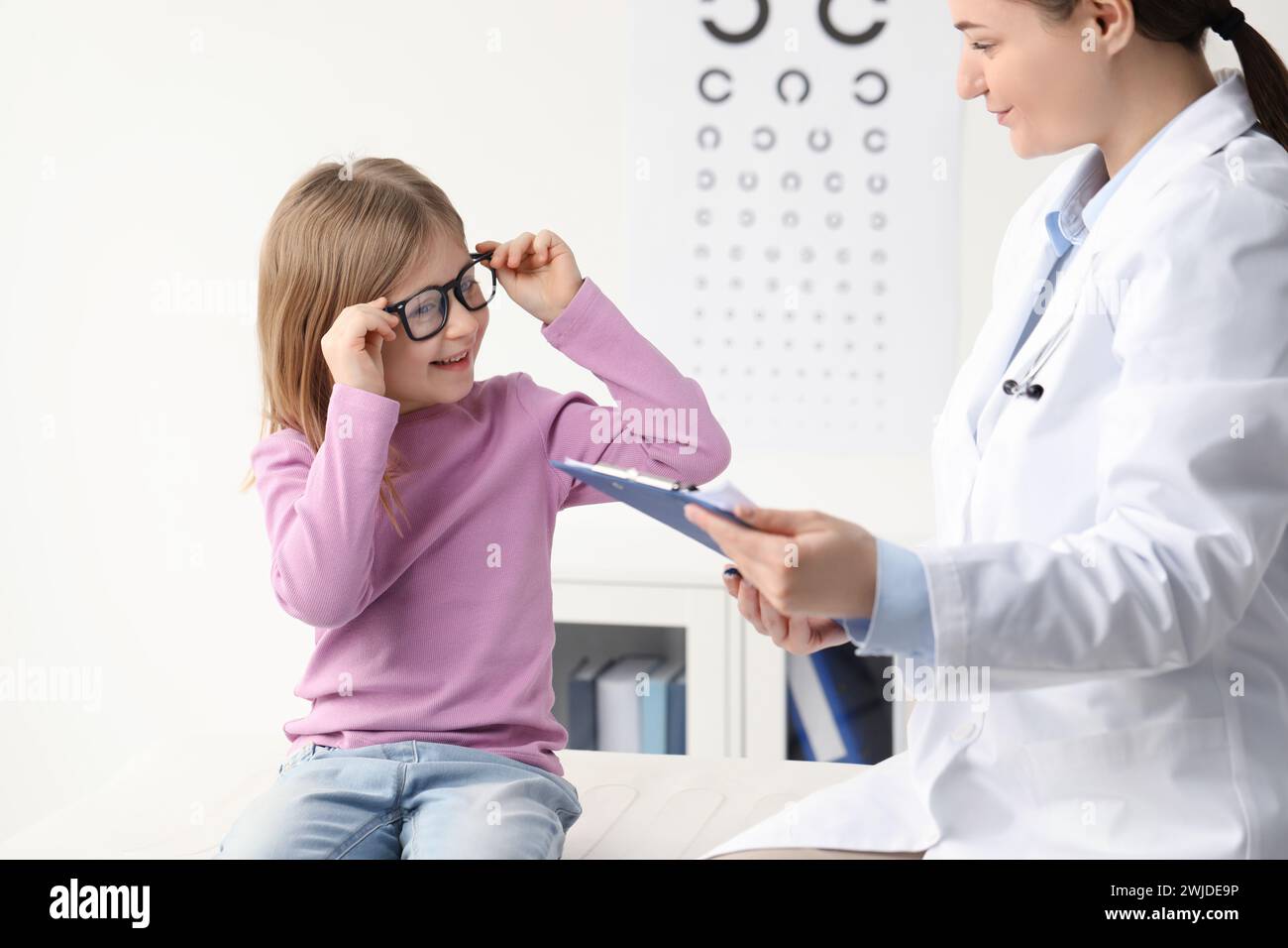 Vision testing. Little girl trying glasses at ophthalmologist office ...