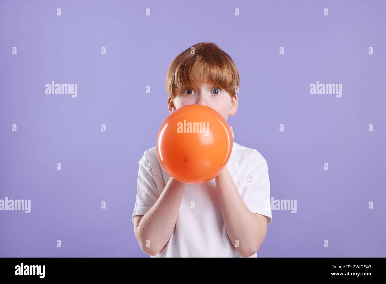 Boy inflating orange balloon on violet background Stock Photo - Alamy