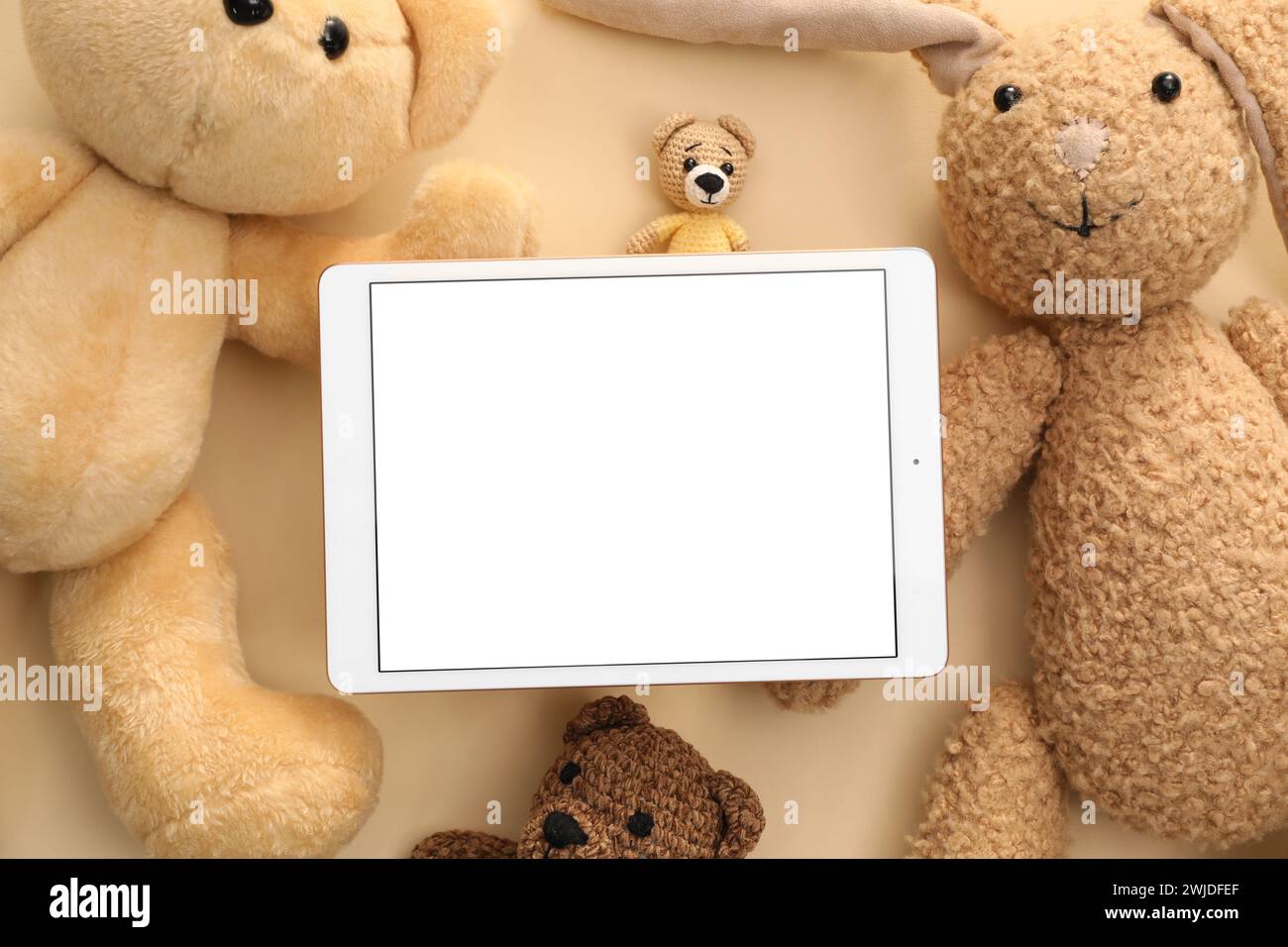 Modern tablet and stuffed animals on beige background, flat lay. Space ...