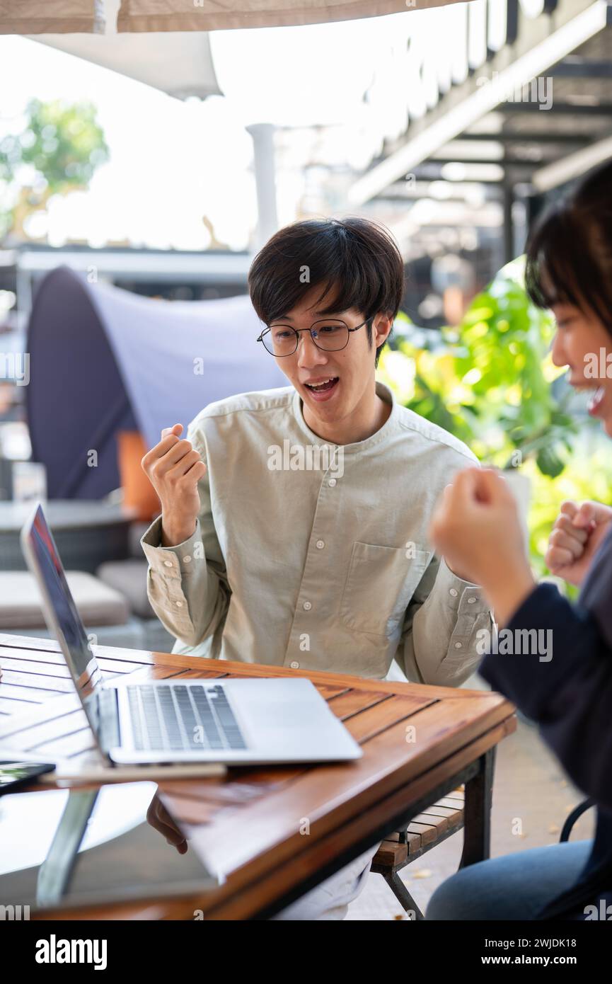 Two excited young Asian colleagues are celebrating their project ...