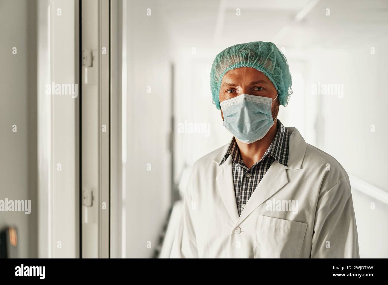 Male doctor in white gown and mask standing in medical clinic and looks ...