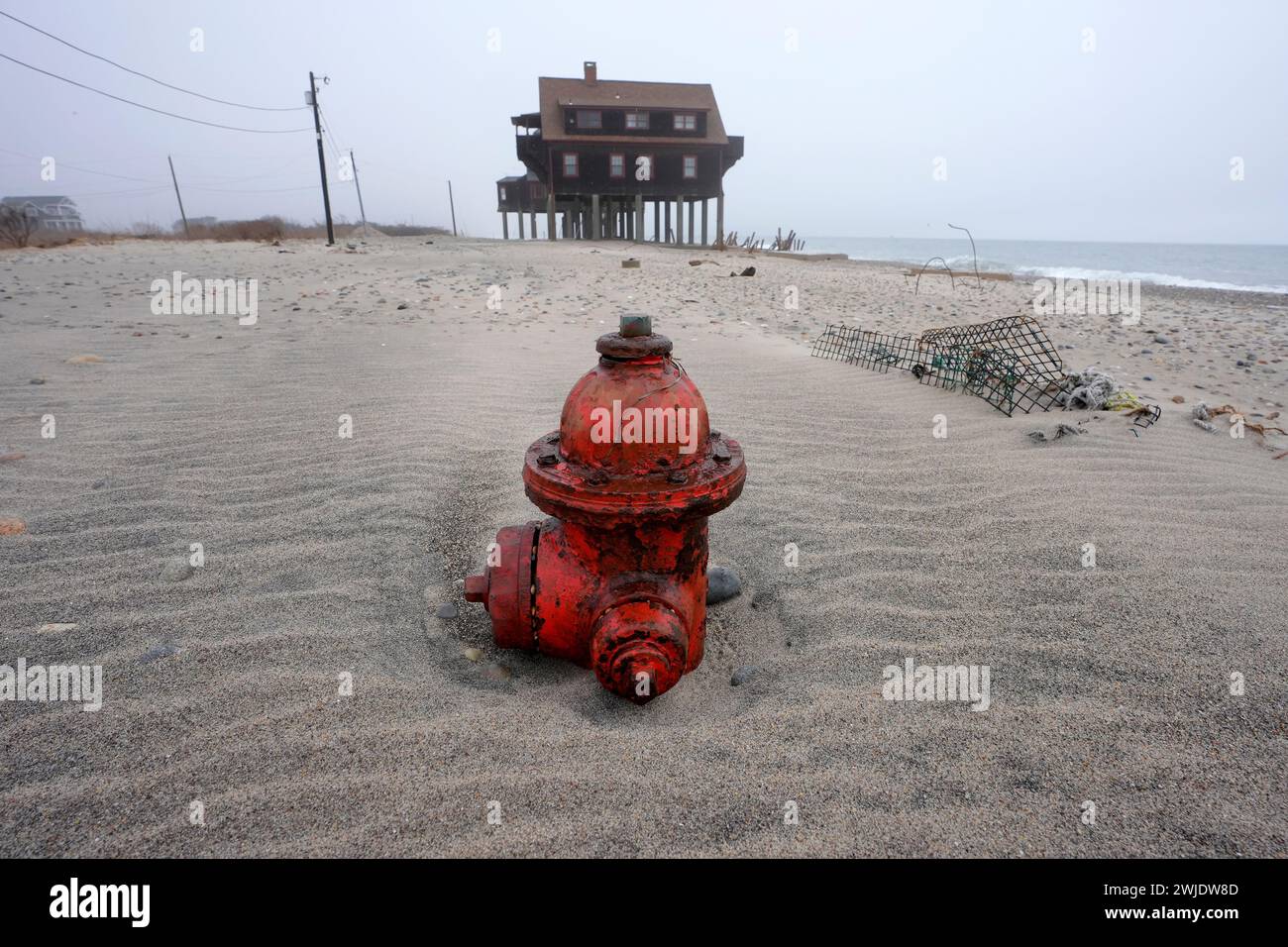A half-buried fire hydrant rests near a house on pylons on the beach ...
