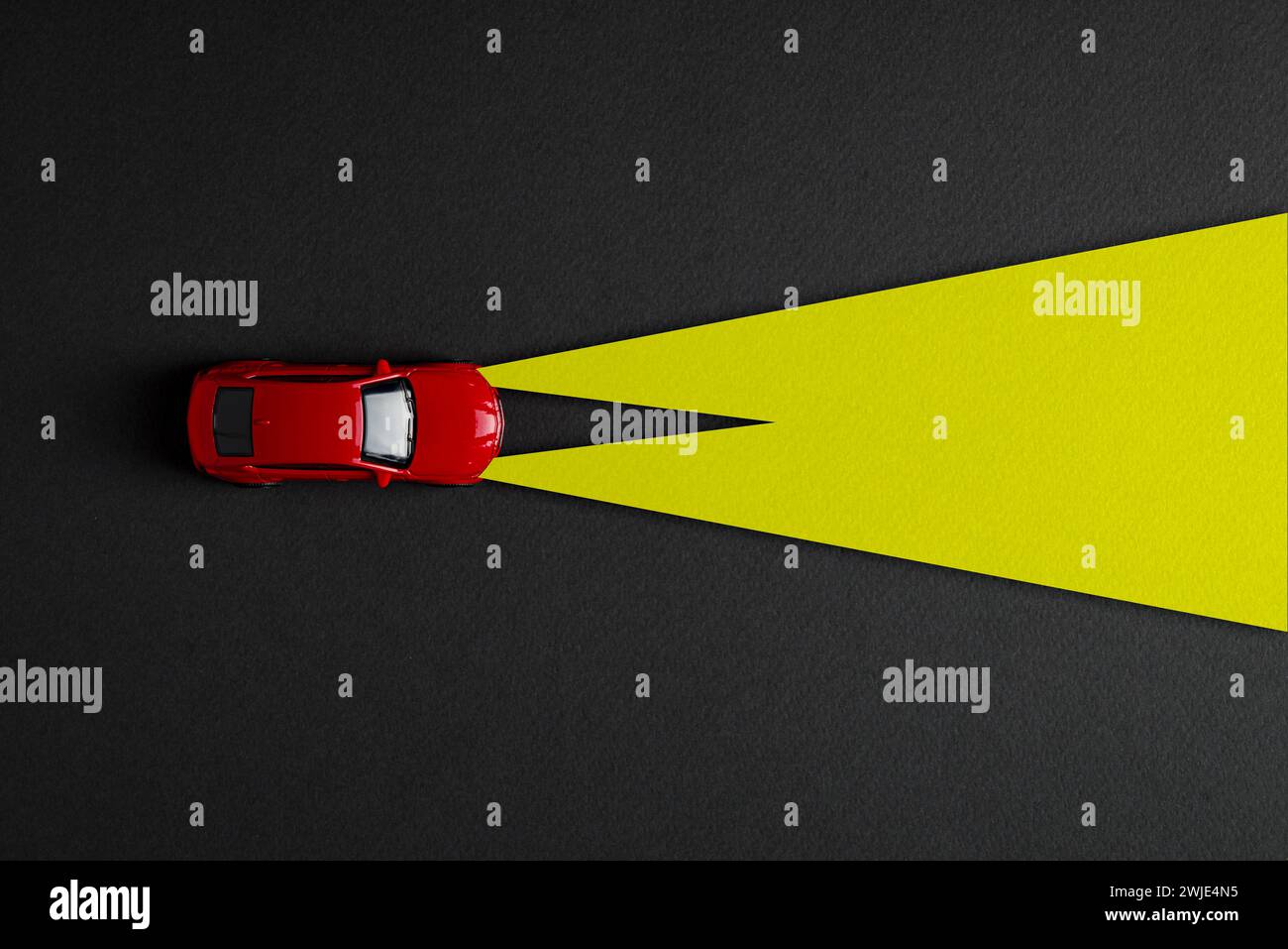 Top view of red toy car and yellow headlights on dark gray background ...