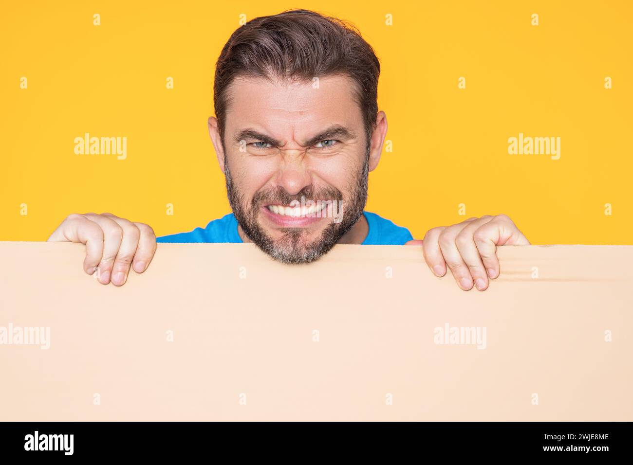 Angry man holding empty board on studio background. Anger guy showing ...