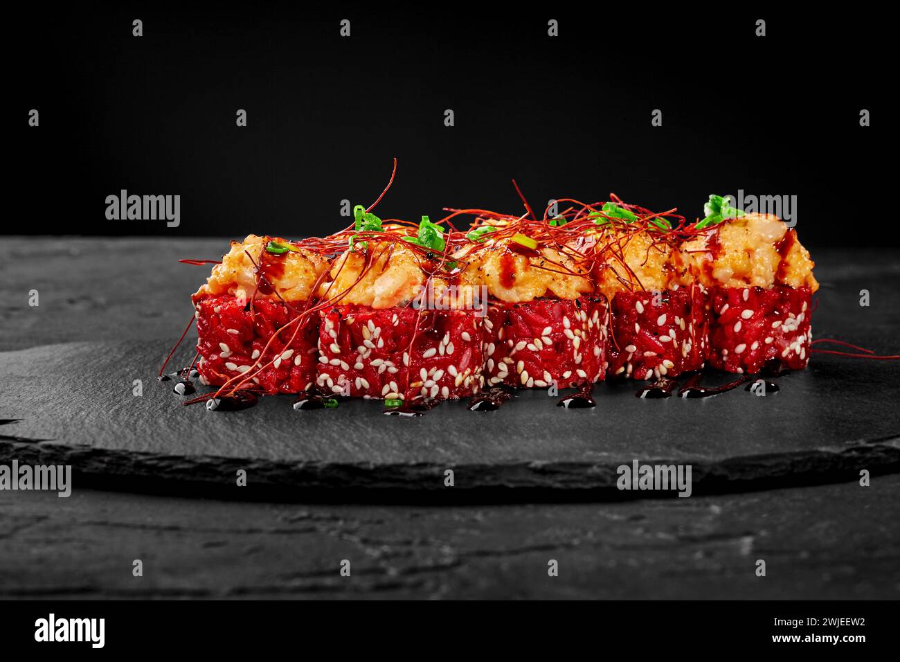 Red rice sushi rolls topped with scallop cheese caps on slate board ...