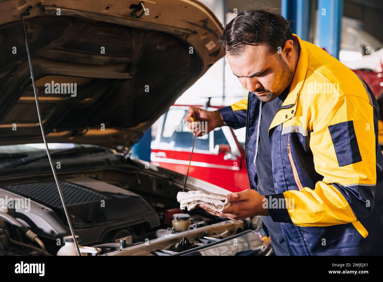 Garage auto mechanic worker working check engine oil level stick in car service center, Indian ...