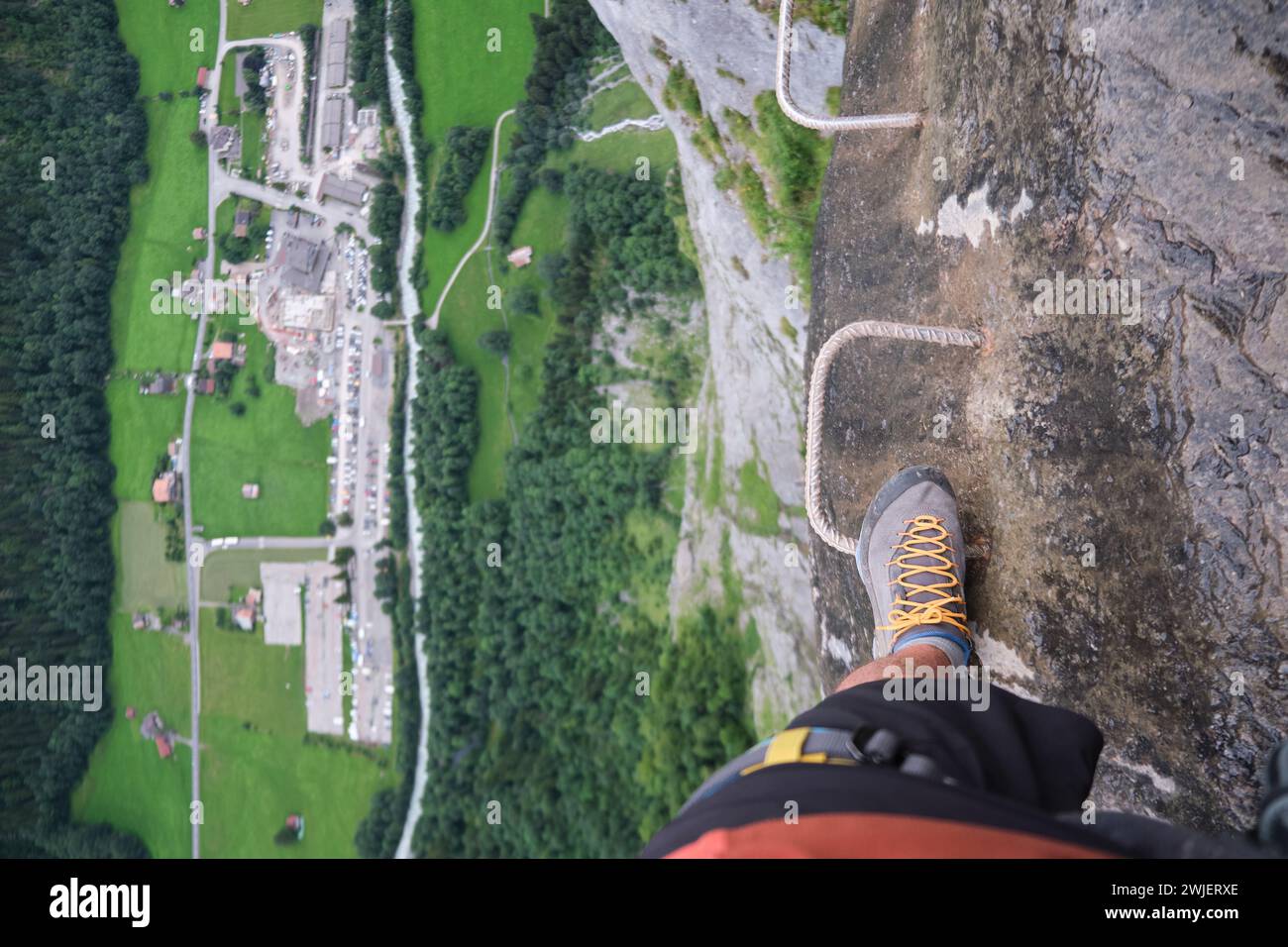 Tourist steps on metal via ferrata brackets, at the edge of a rock wall ...