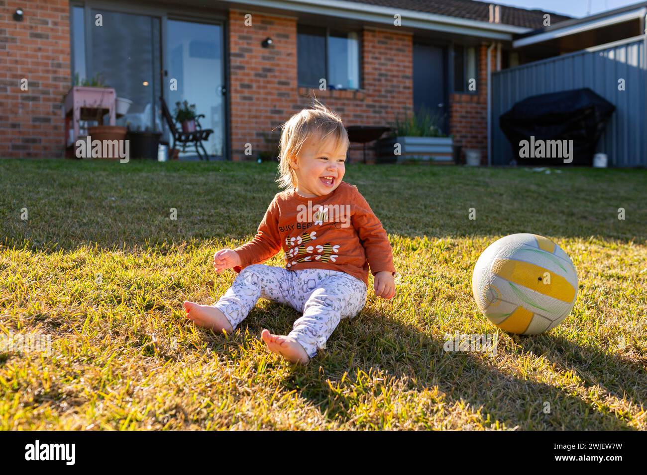 Little kid playing with ball in backyard laughing and rolling it down ...