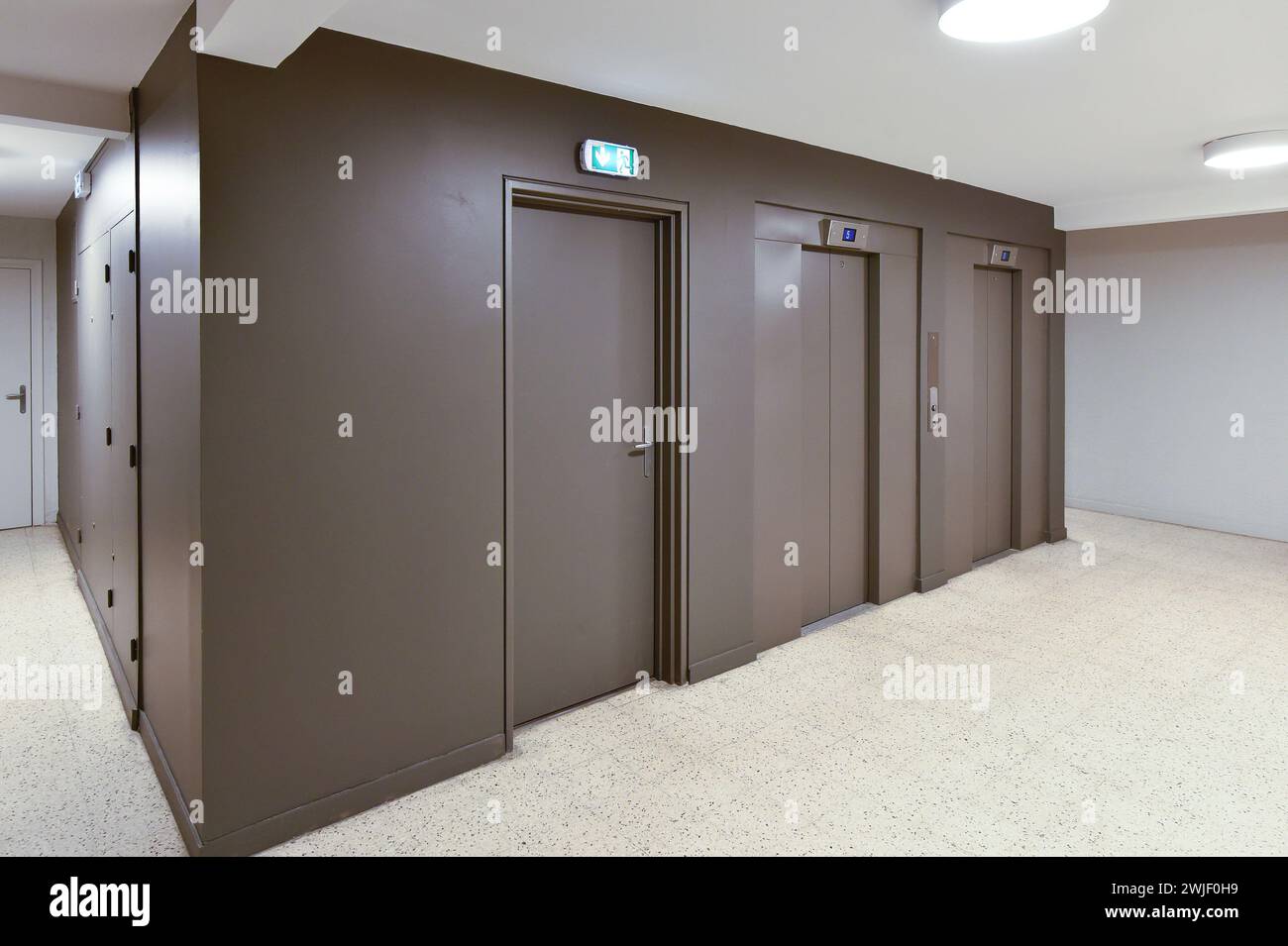Two brown lifts and door to the service staircase in the lobby of a ...