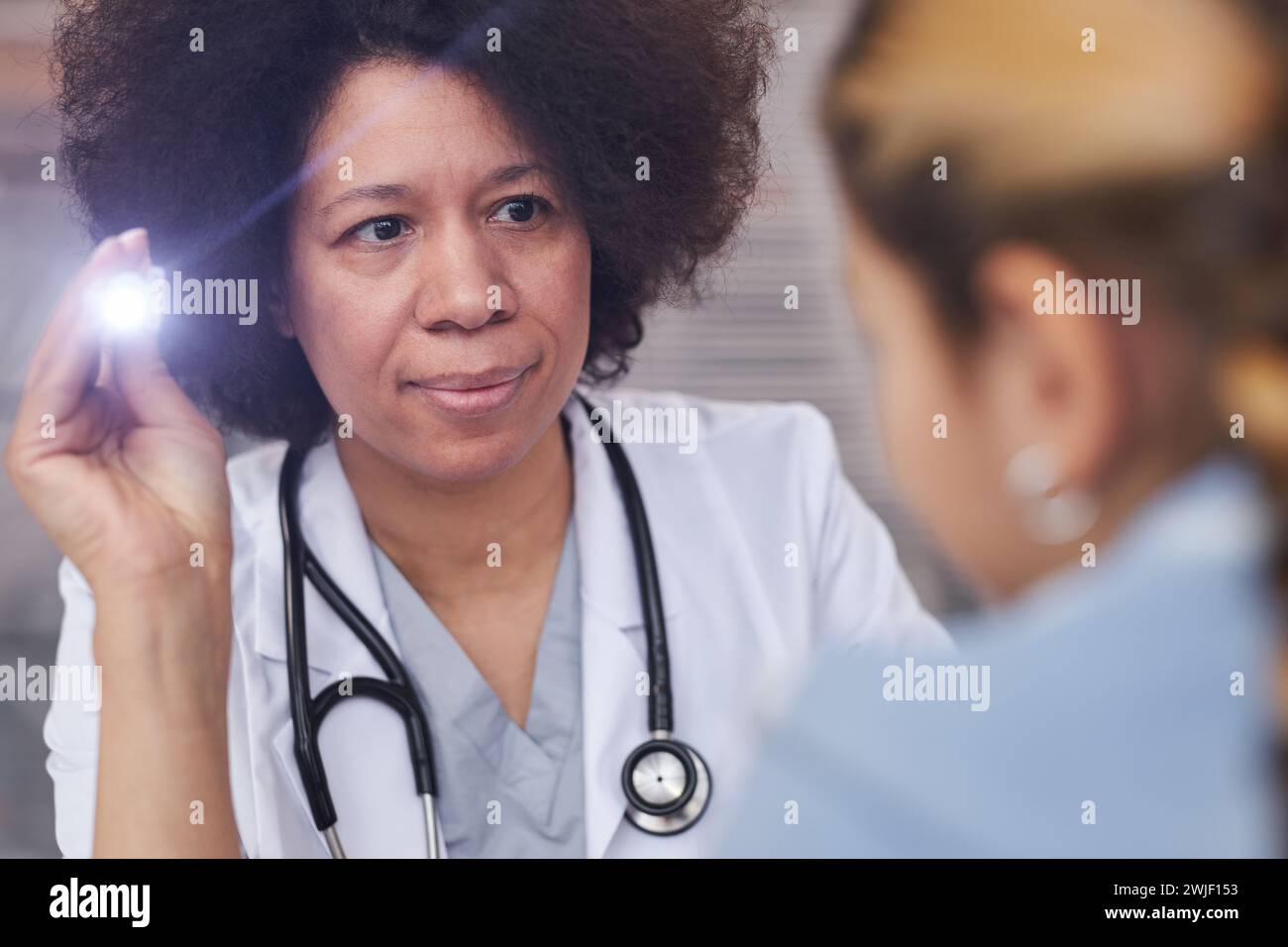 Portrait of smiling African American doctor using pen light while ...