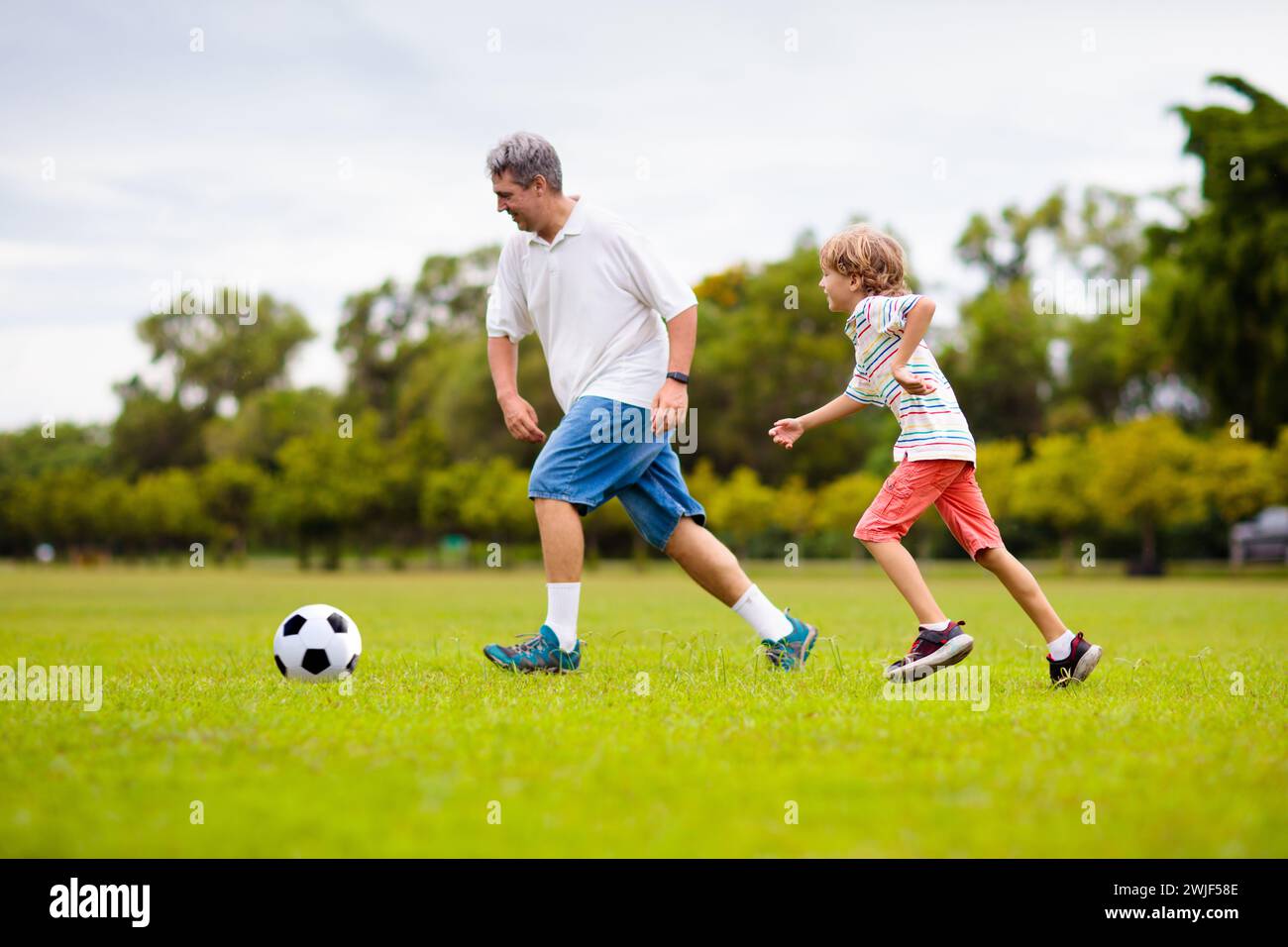 Father and son play football on outdoor pitch. Dad and kid run on park ...