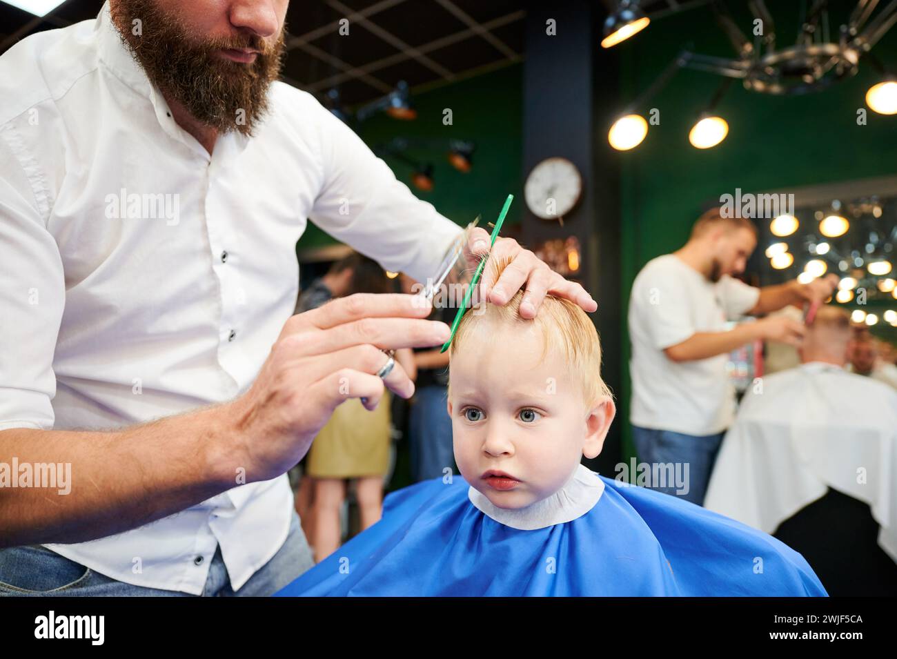 Man barber cutting little boy's hair using comb and scissors. Child ...