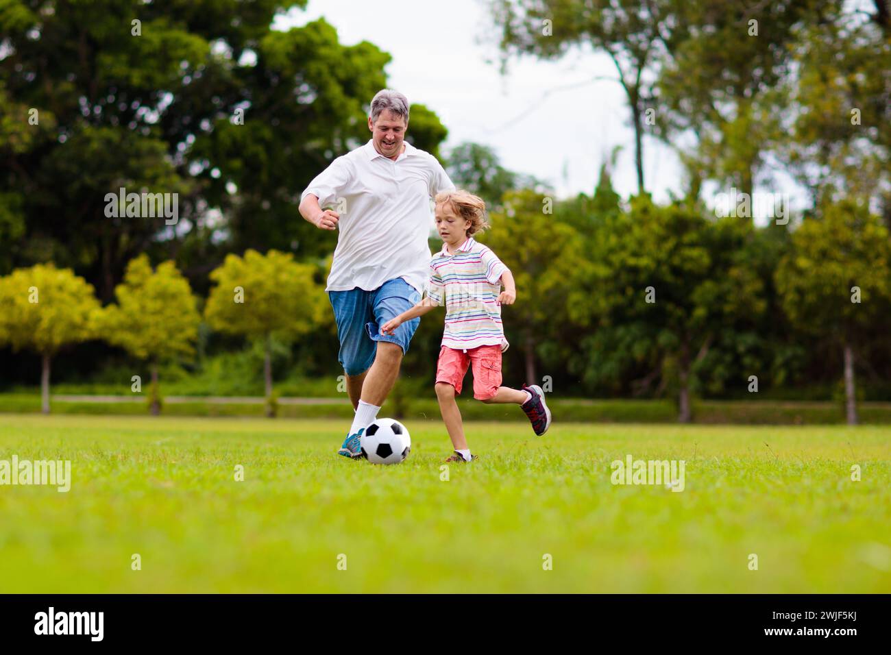 Father and son play football on outdoor pitch. Dad and kid run on park ...