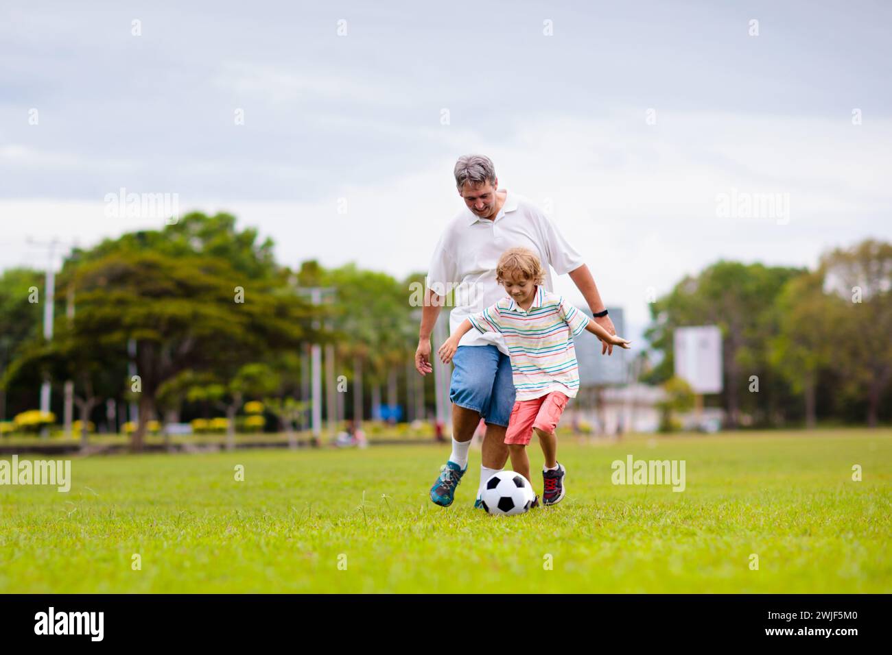 Father and son play football on outdoor pitch. Dad and kid run on park ...