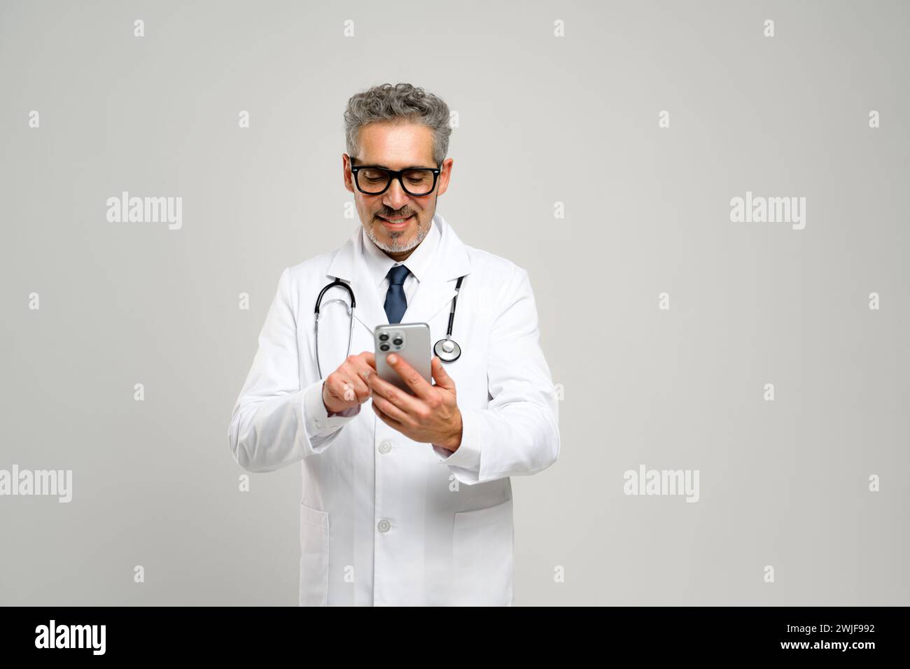 A senior doctor with a friendly demeanor is holding a smartphone ...