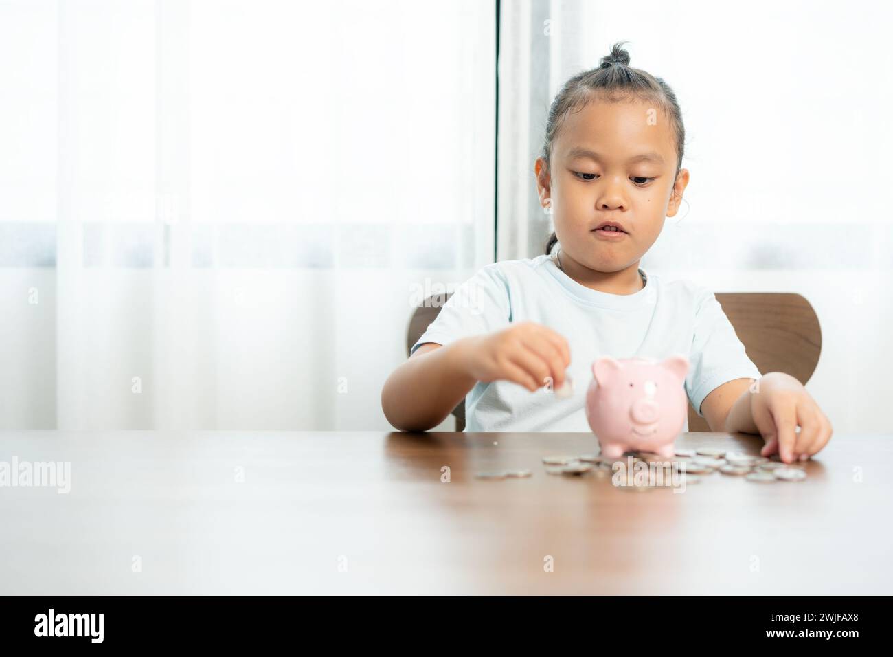 A girl saving money, putting coins into a piggy bank for the future ...